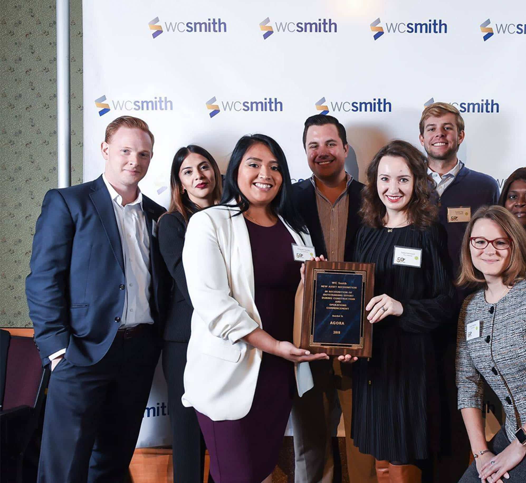 A group of people stands indoors holding an award plaque, proudly ...